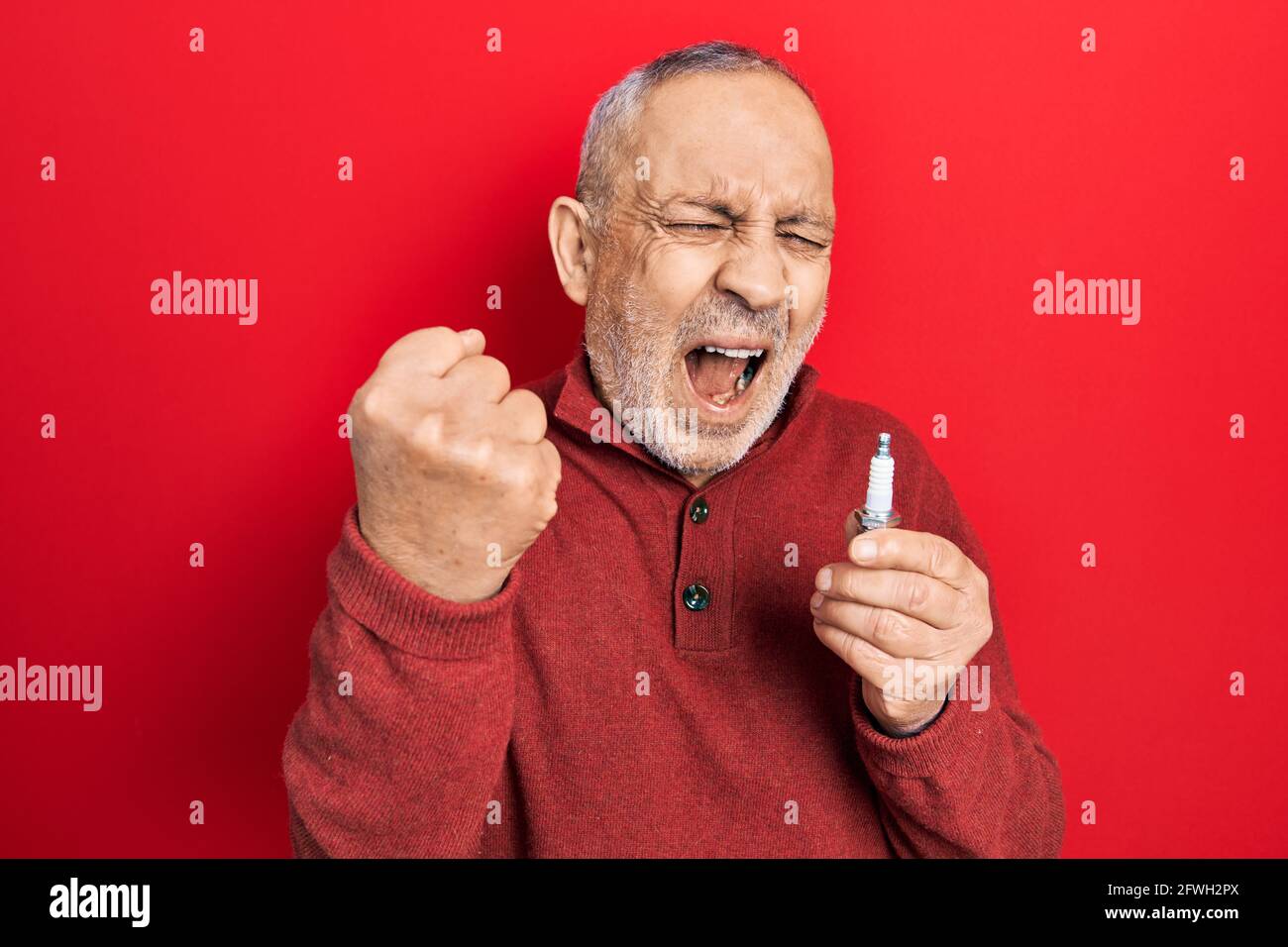 Handsome mature man holding spark plug annoyed and frustrated shouting ...