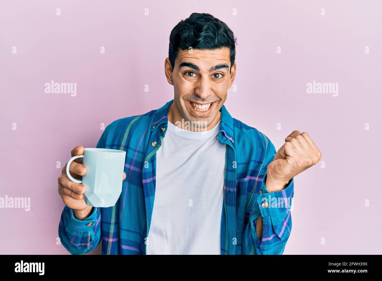 Handsome hispanic man drinking a cup of coffee screaming proud ...