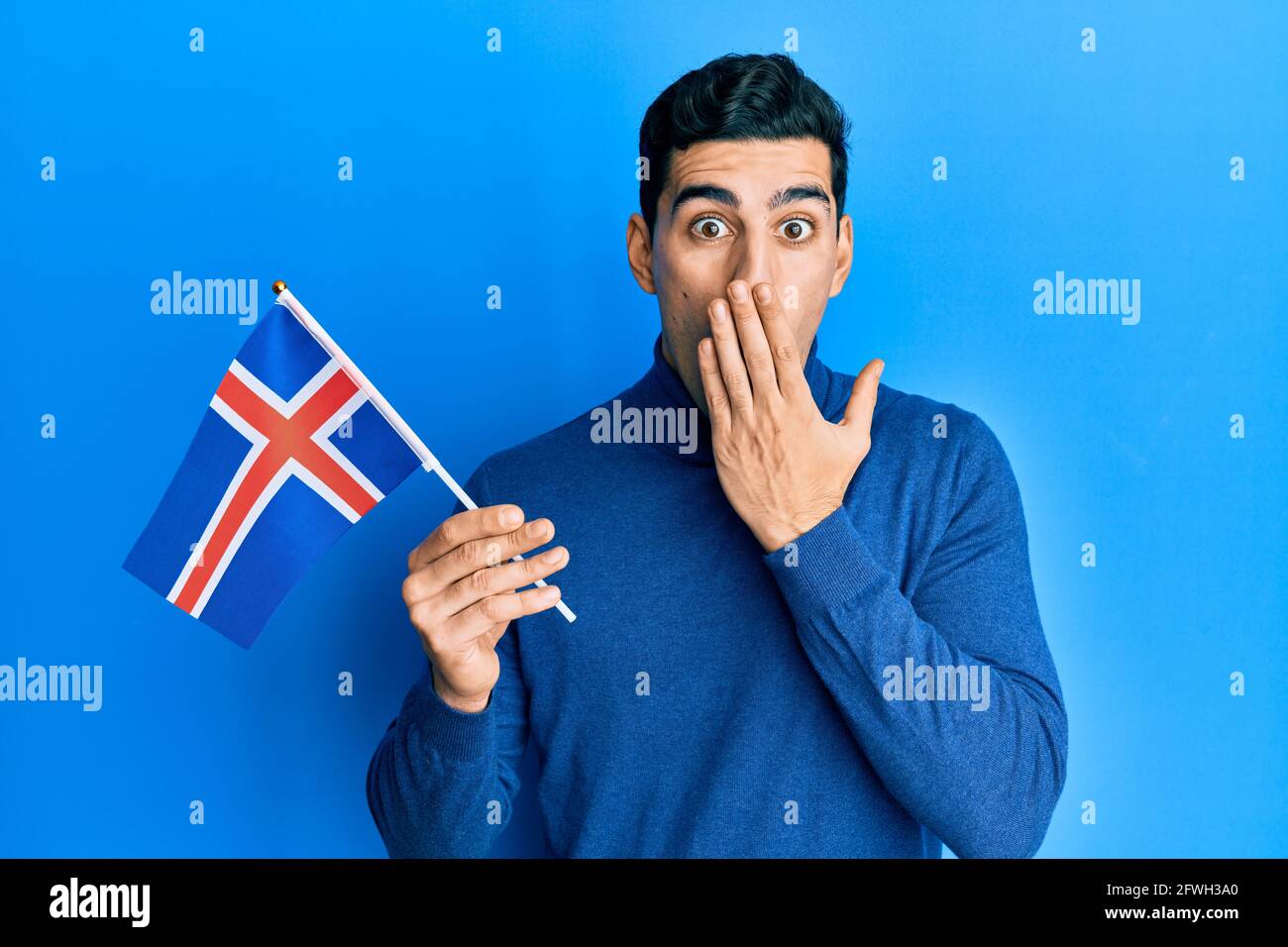 Handsome hispanic man holding island flag covering mouth with hand ...