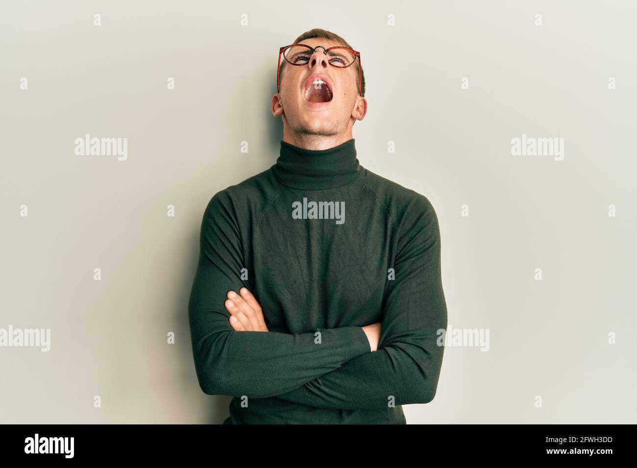 Young caucasian man wearing glasses with arms crossed gesture angry and ...