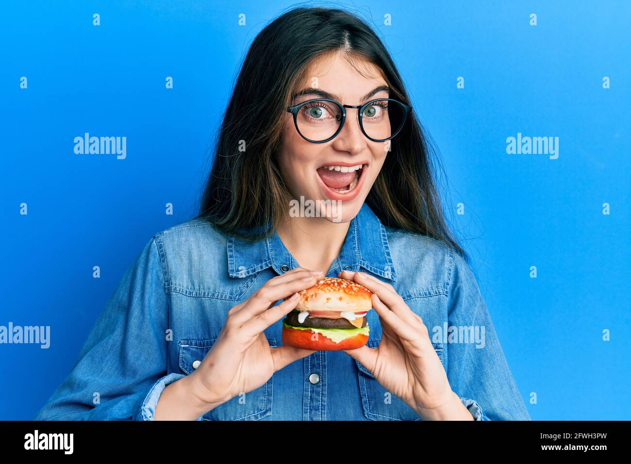 Young caucasian woman eating a tasty classic burger celebrating crazy ...