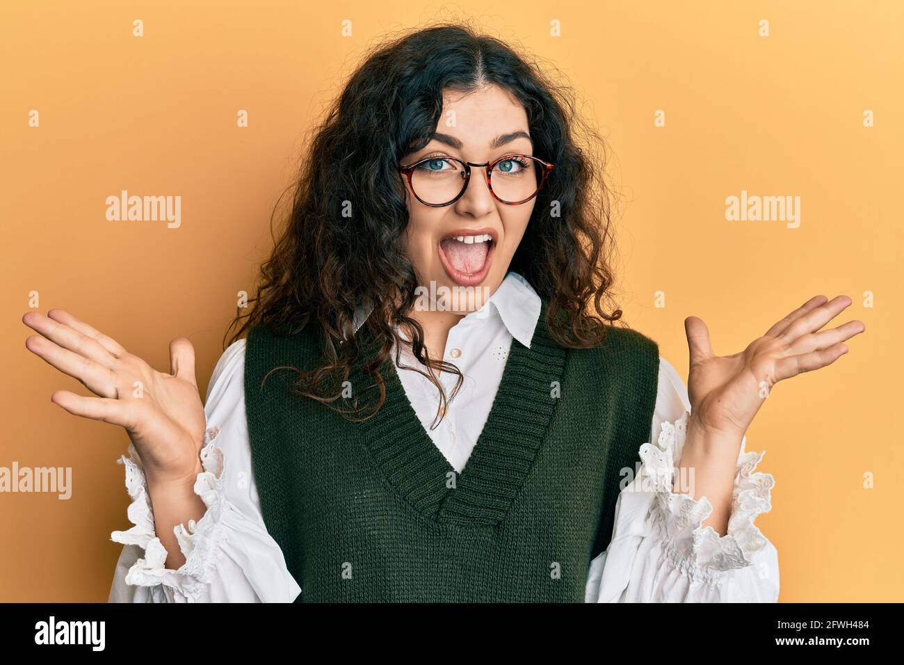 Young brunette woman with curly hair wearing casual clothes and glasses ...