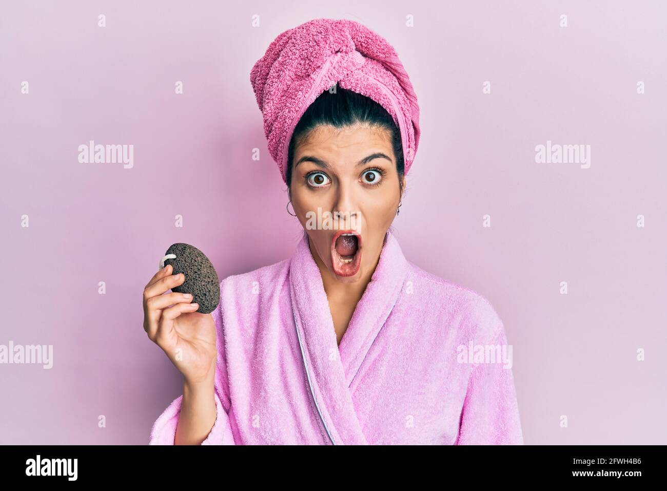 Young hispanic woman wearing shower bathrobe holding pumice stone ...