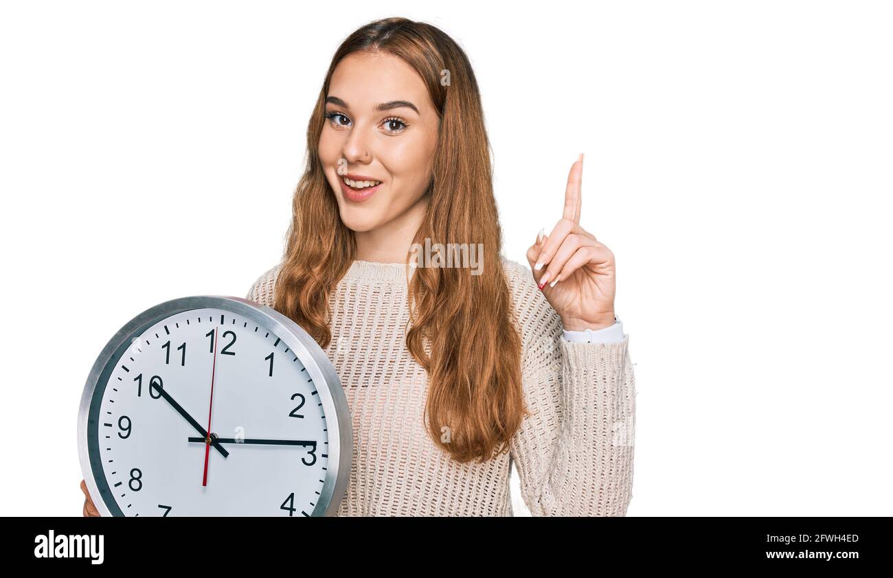 Young blonde woman holding big clock surprised with an idea or question ...