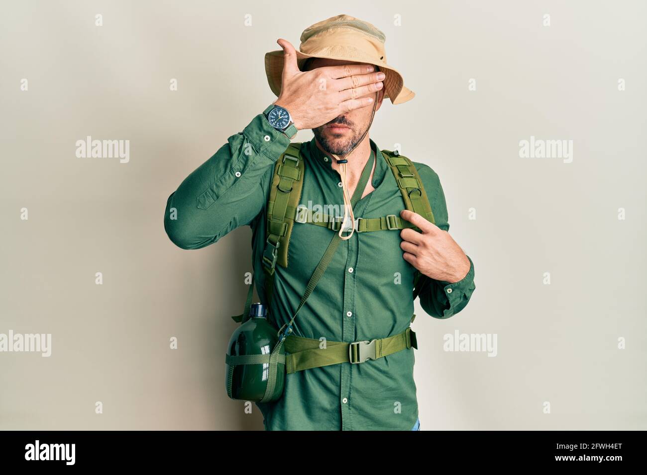 Handsome man with beard wearing explorer hat and backpack covering eyes ...