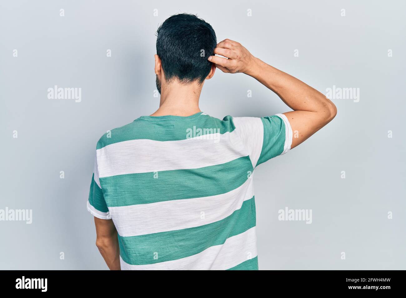 Young hispanic man wearing casual clothes backwards thinking about ...