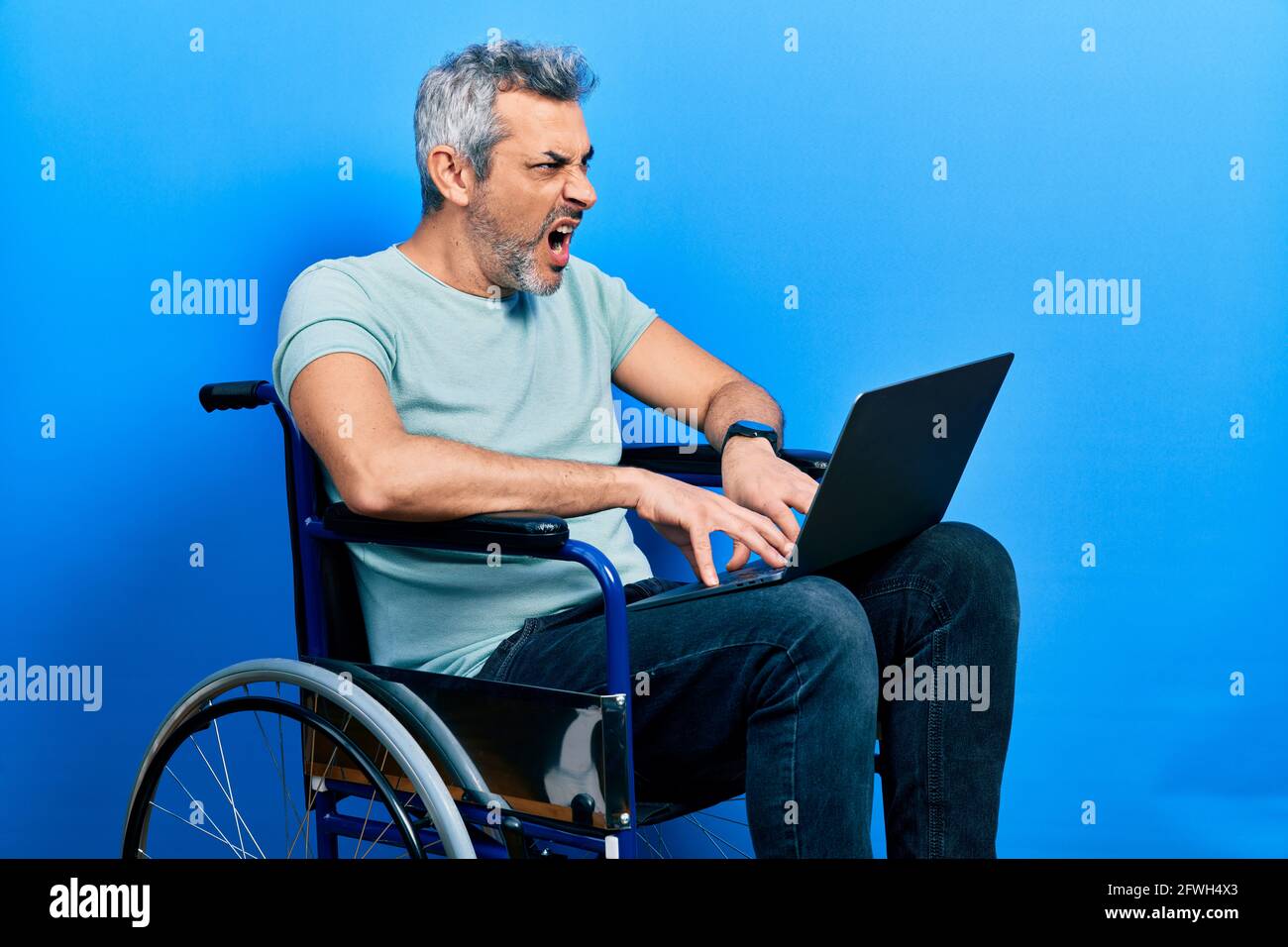 Handsome middle age man with grey hair sitting on wheelchair using ...
