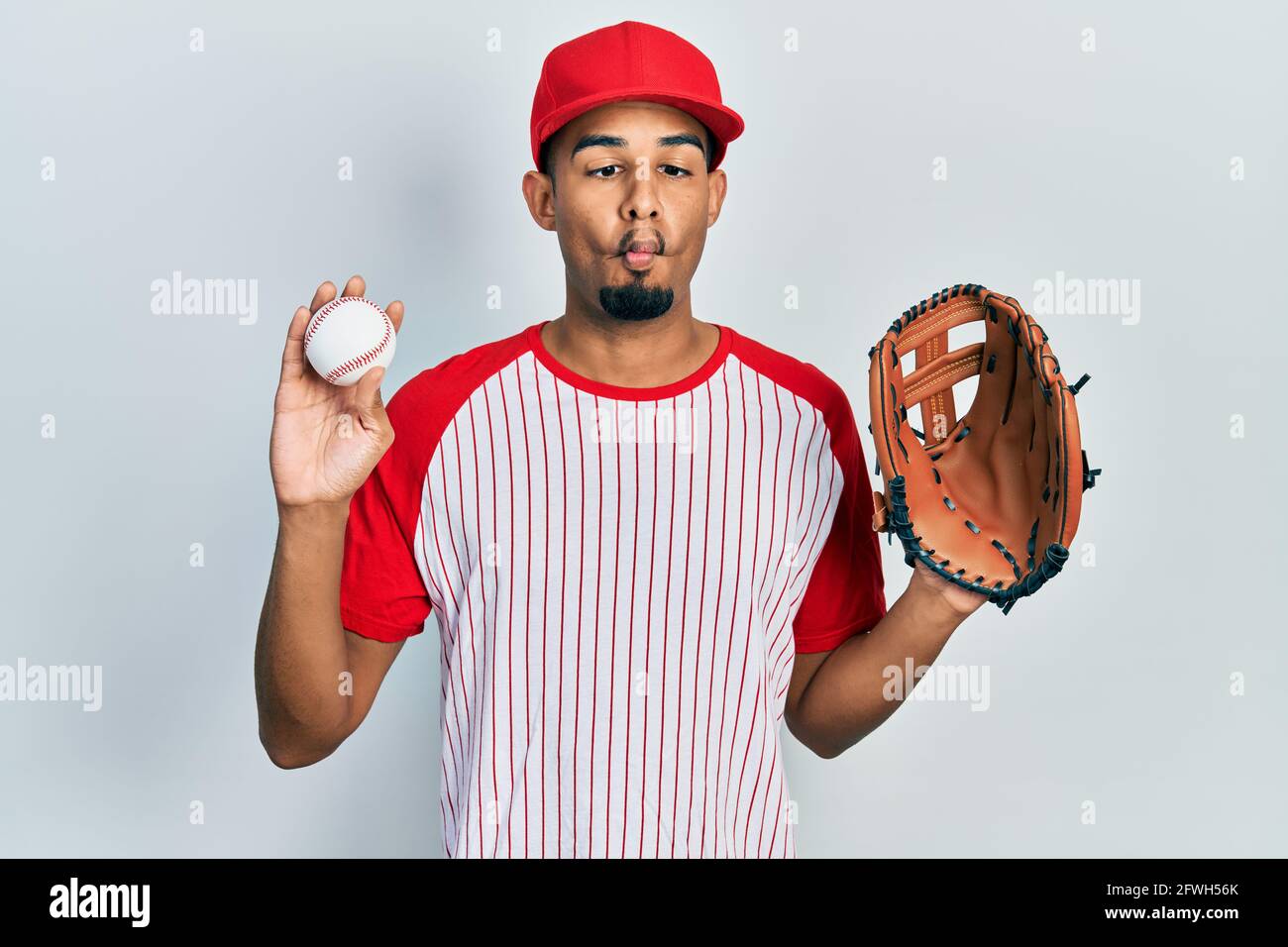 Young african american man wearing baseball uniform holding glove and ...