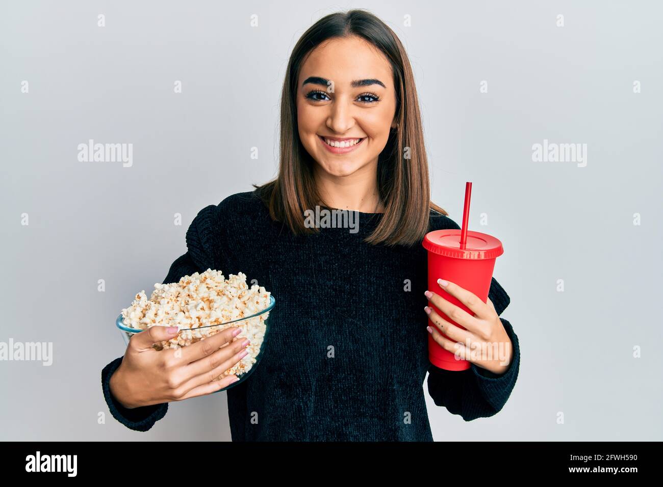 Young brunette girl eating popcorn and drinking soda smiling with a ...