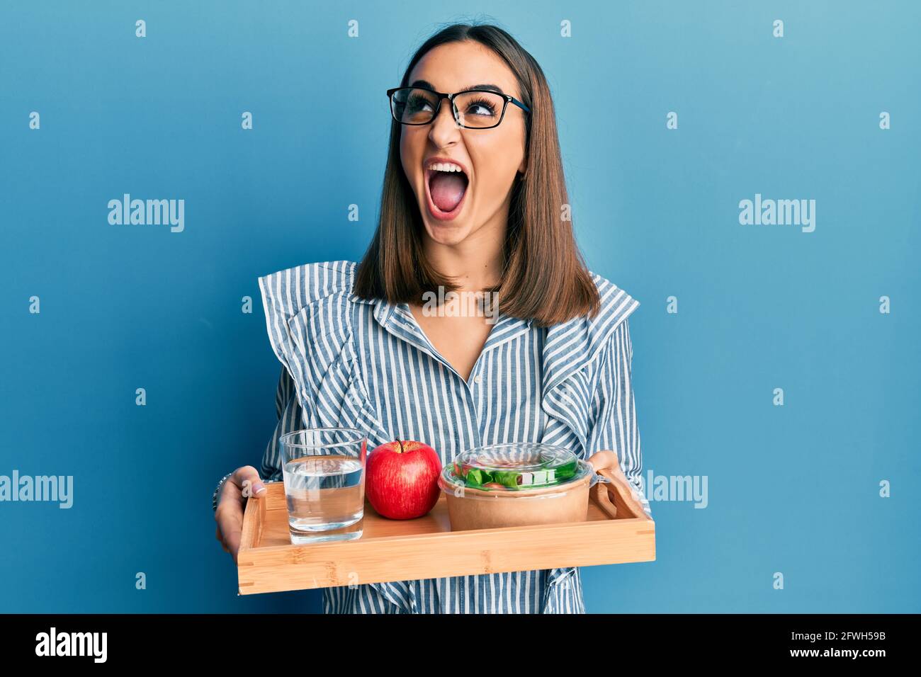 Young brunette girl holding tray with healthy lunch angry and mad ...