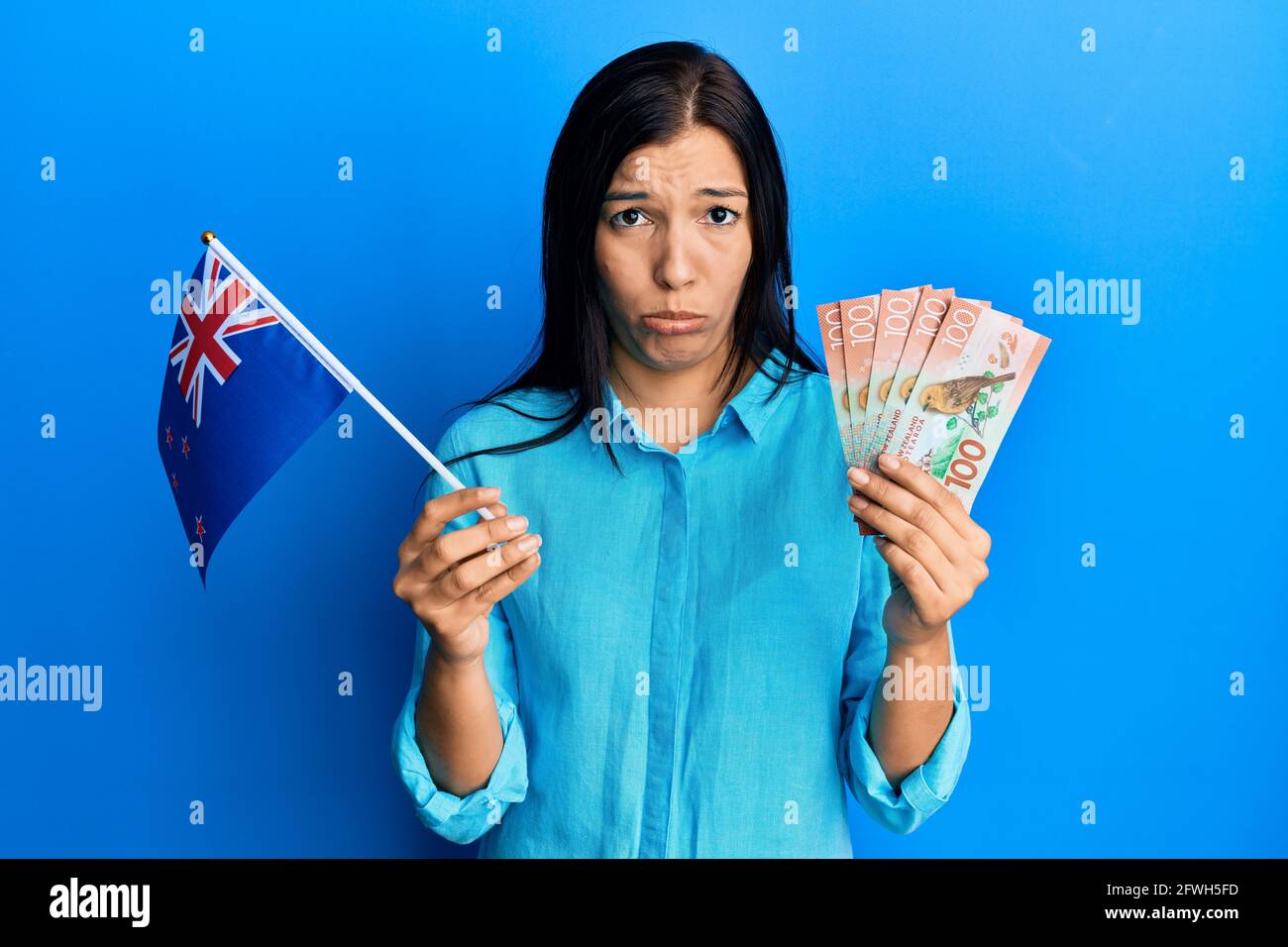 Young latin woman holding new zealand flag and dollars depressed and ...