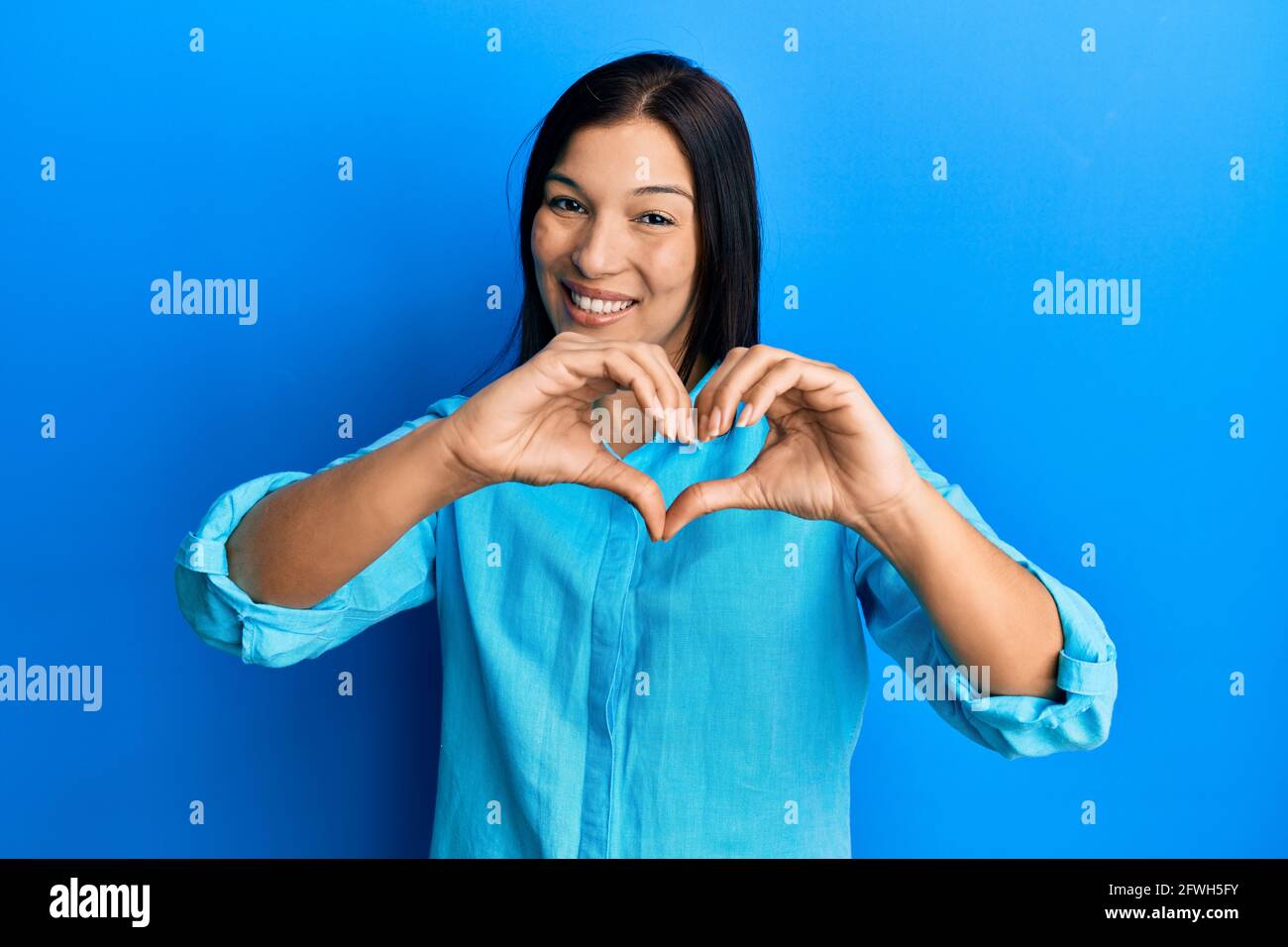 Young latin woman wearing casual clothes smiling in love doing heart ...