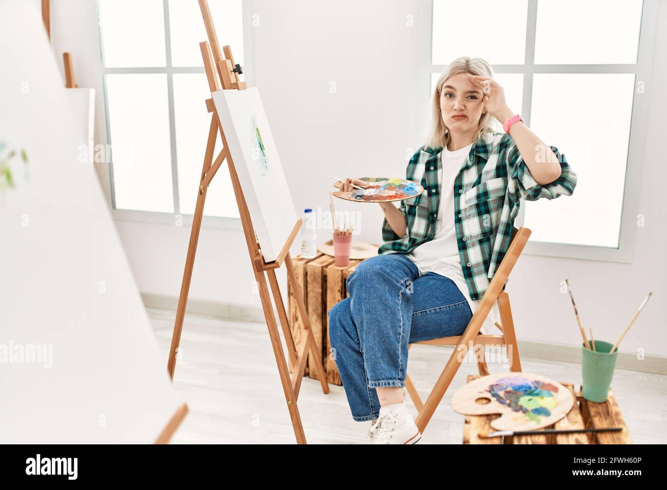Young artist woman painting on canvas at art studio worried and ...