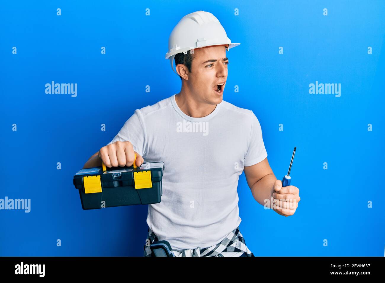 Handsome young man holding toolbox and screwdriver angry and mad ...