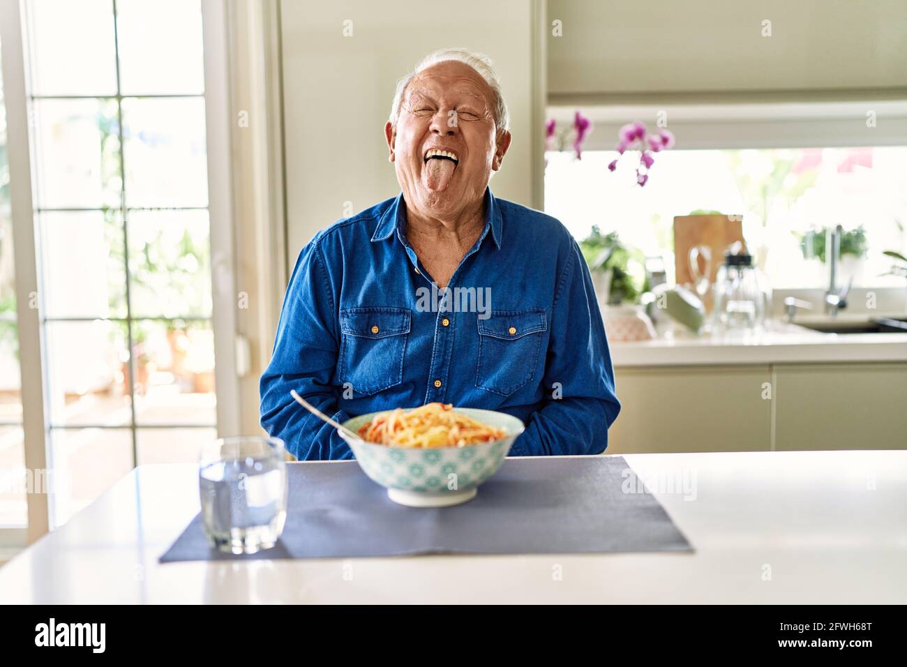 Senior man with grey hair eating pasta spaghetti at home sticking ...