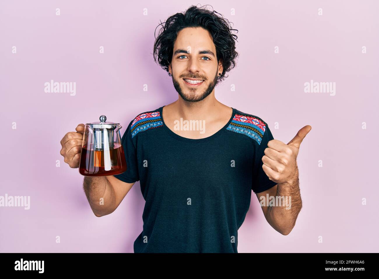 Handsome hispanic man holding traditional tea pot smiling happy and ...