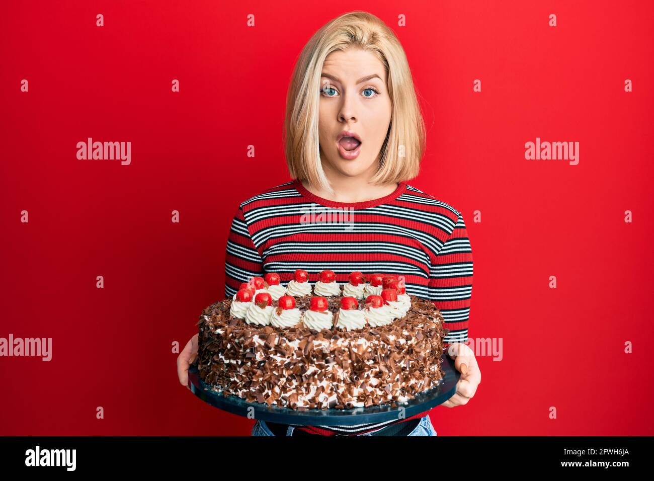Young blonde woman celebrating birthday holding big chocolate cake in ...