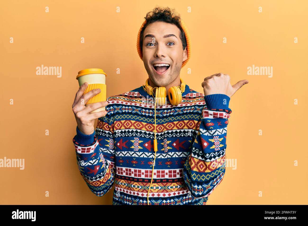Young handsome man drinking cup of coffee wearing headphones pointing ...