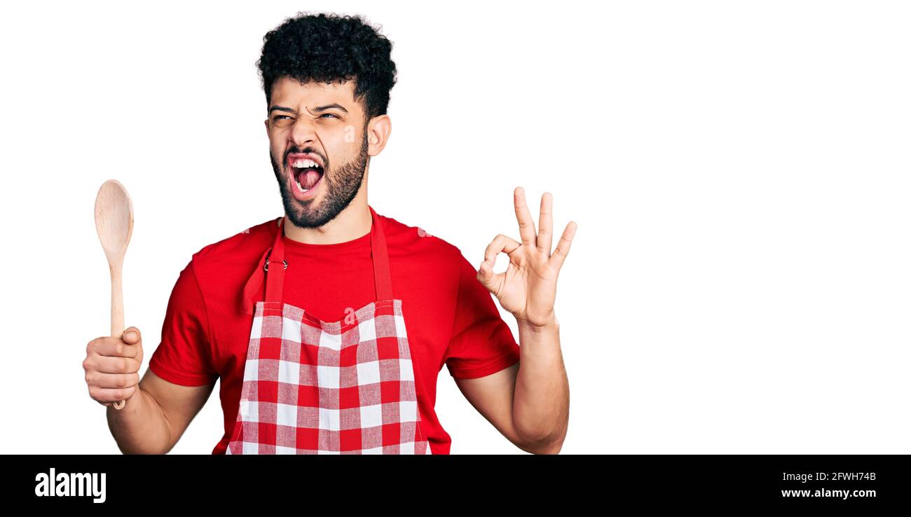 Young arab man with beard wearing baker uniform holding wooden spoon ...