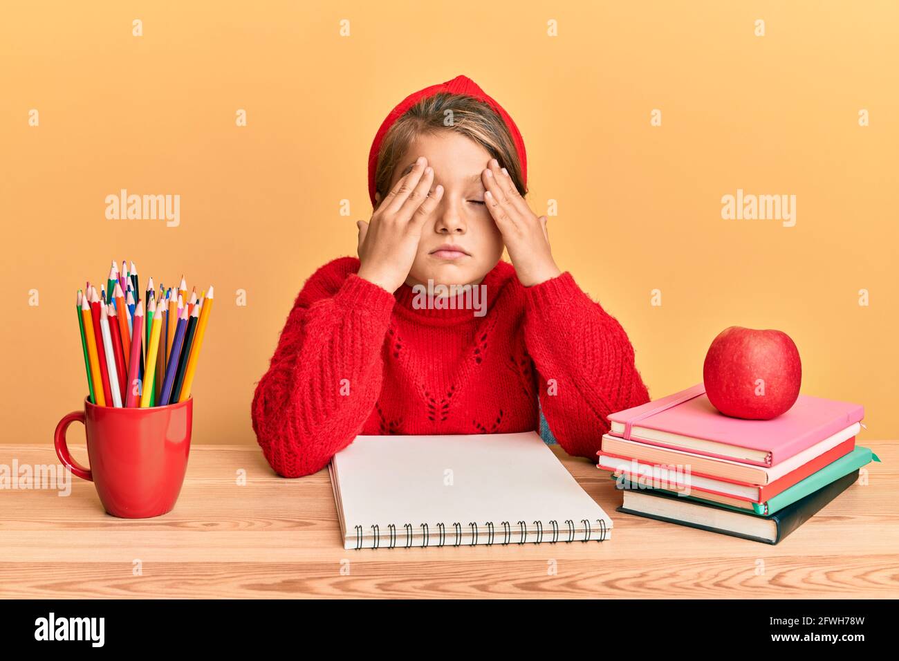 Little beautiful girl sitting on classroom desk suffering from headache ...