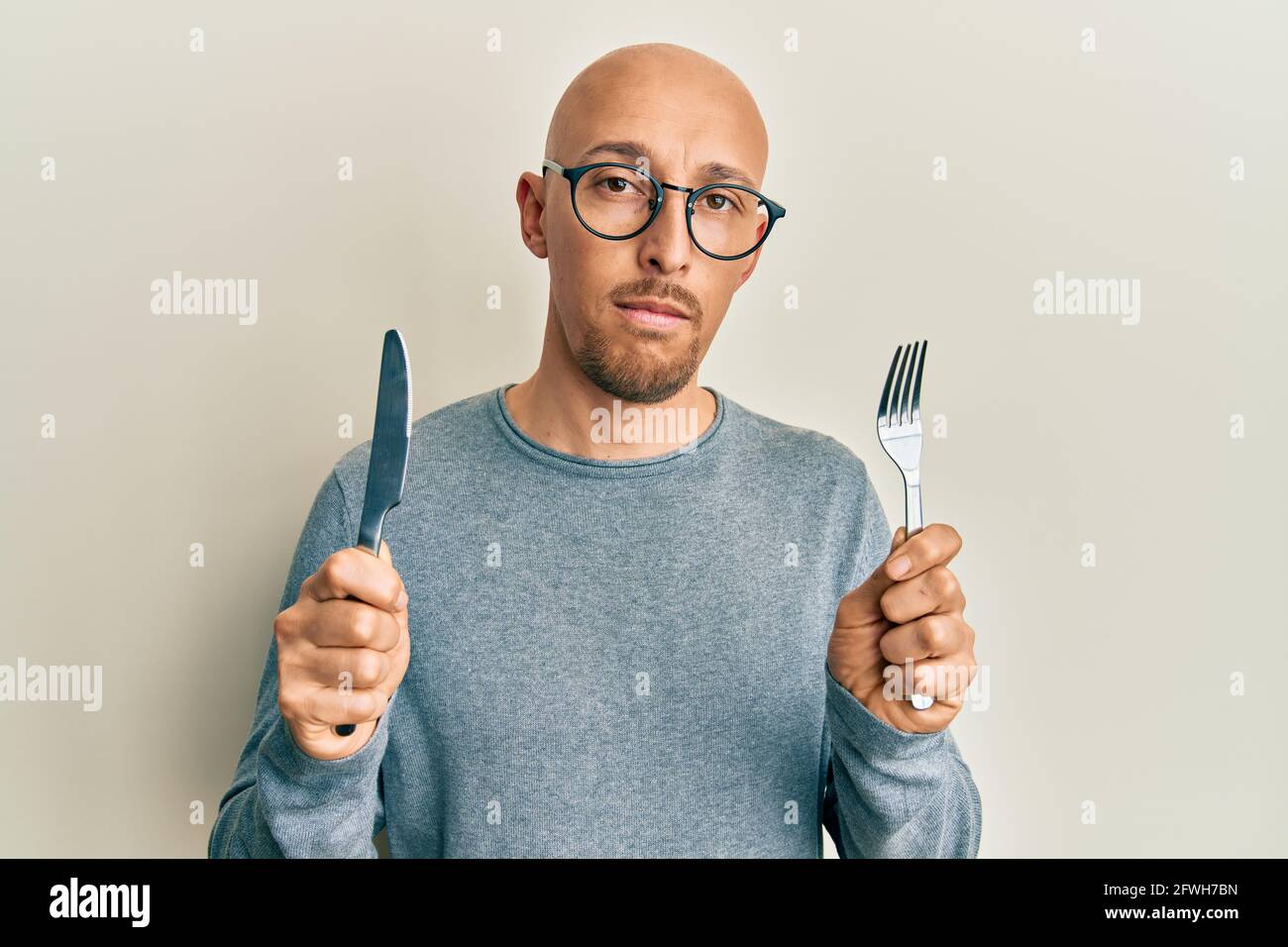 Bald man with beard holding fork and knife ready to eat relaxed with ...