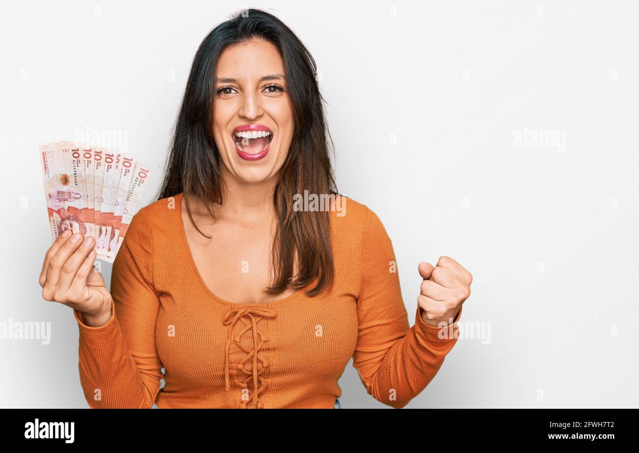 Beautiful hispanic woman holding 10 colombian pesos banknotes screaming ...