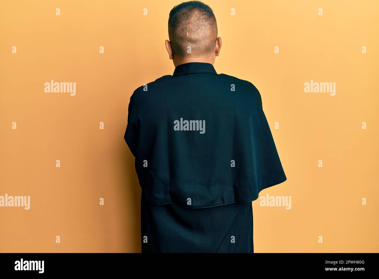 Young latin priest man standing over yellow background standing ...