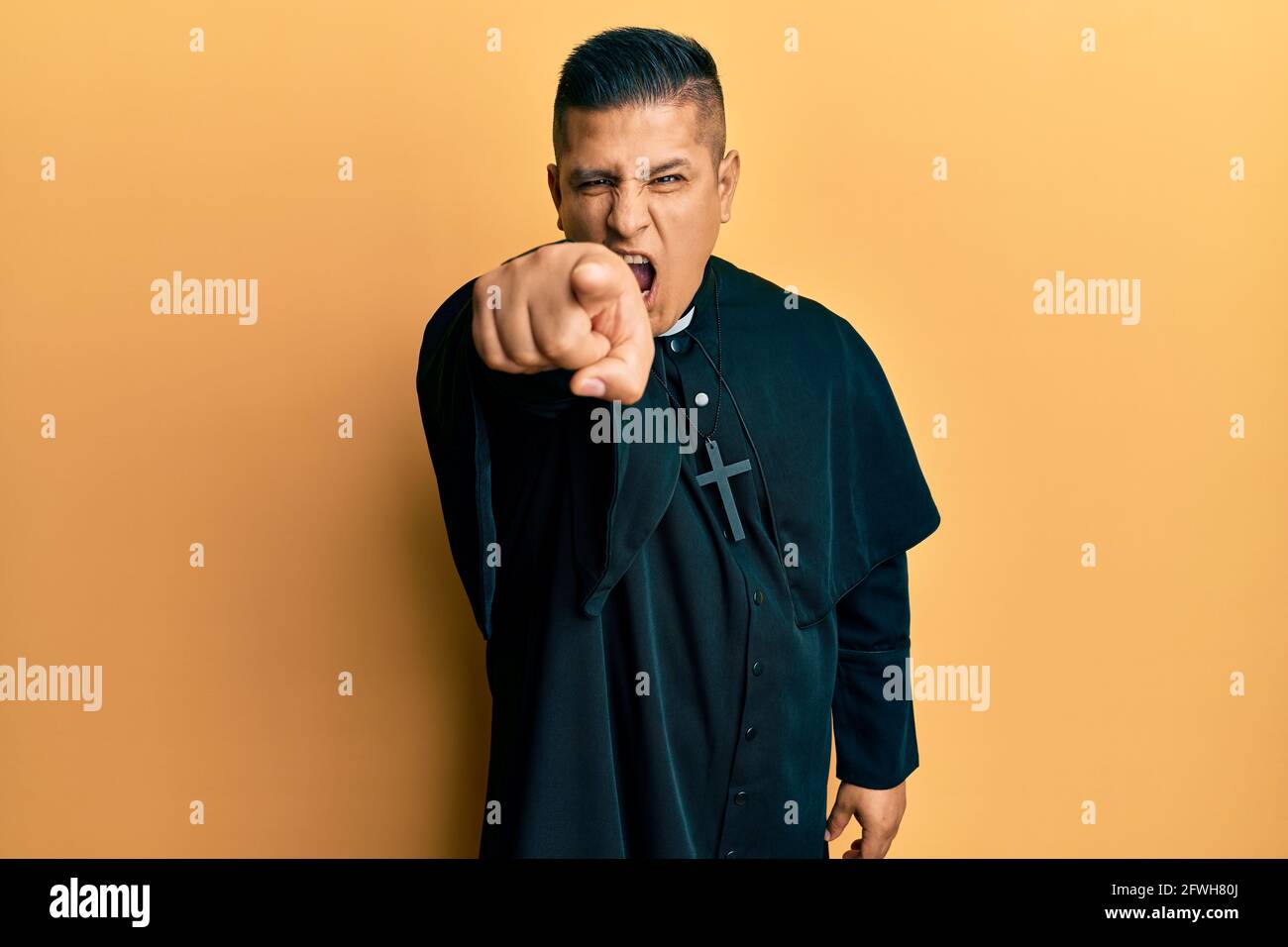 Young latin priest man standing over yellow background pointing ...