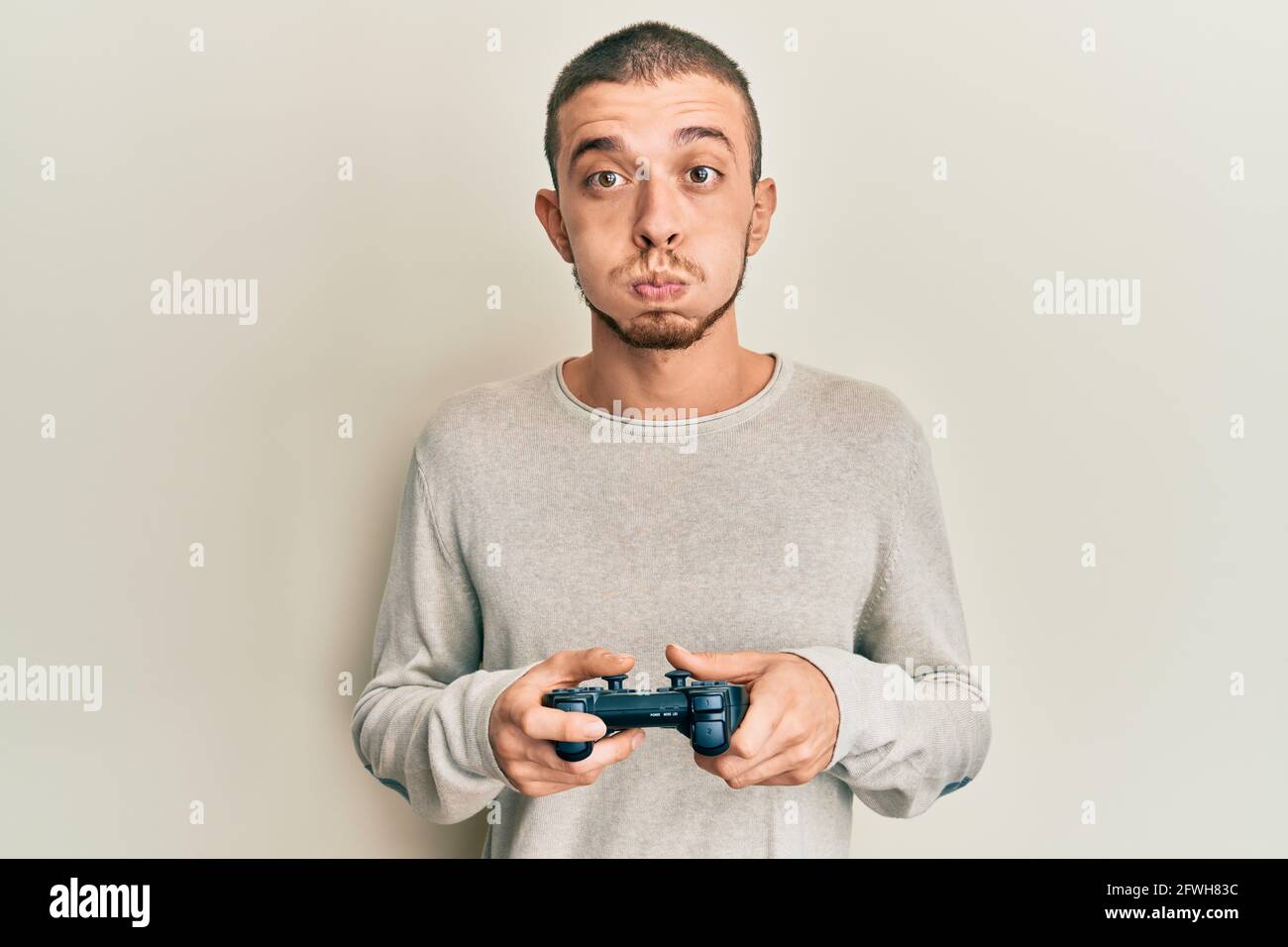 Hispanic young man playing video game holding controller puffing cheeks ...