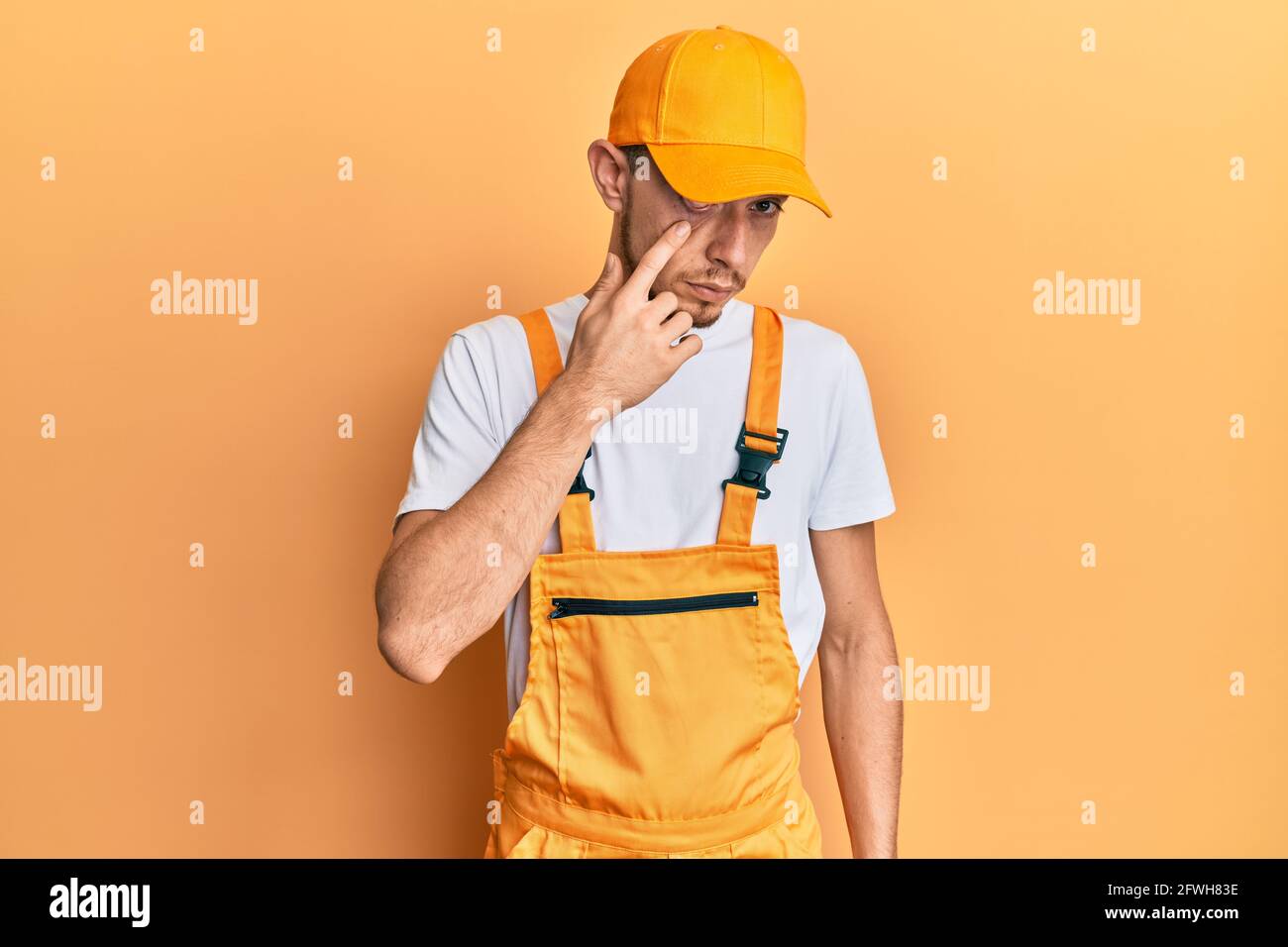 Hispanic young man wearing handyman uniform pointing to the eye ...