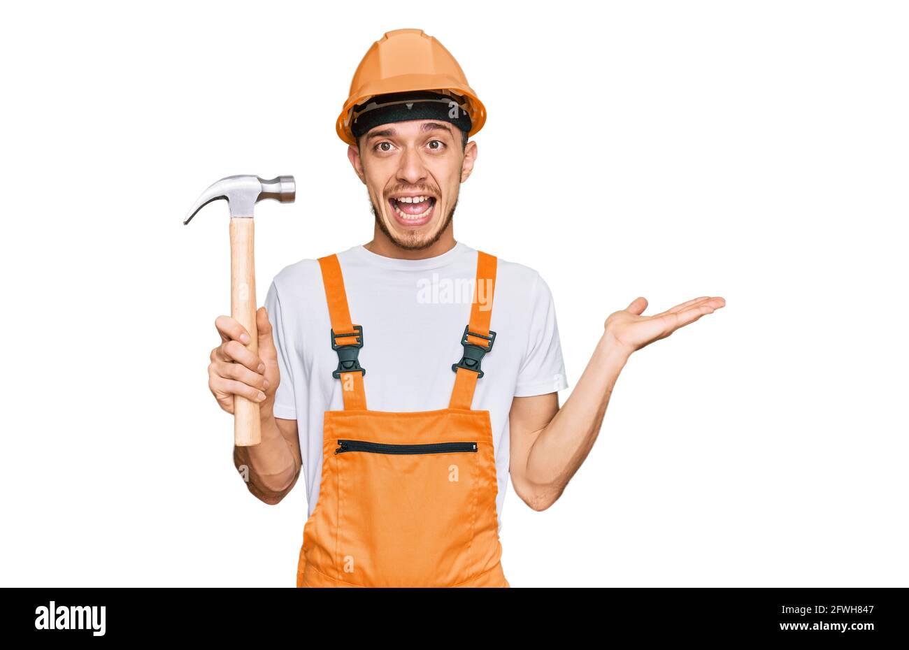 Hispanic young man wearing hardhat holding hammer celebrating victory ...