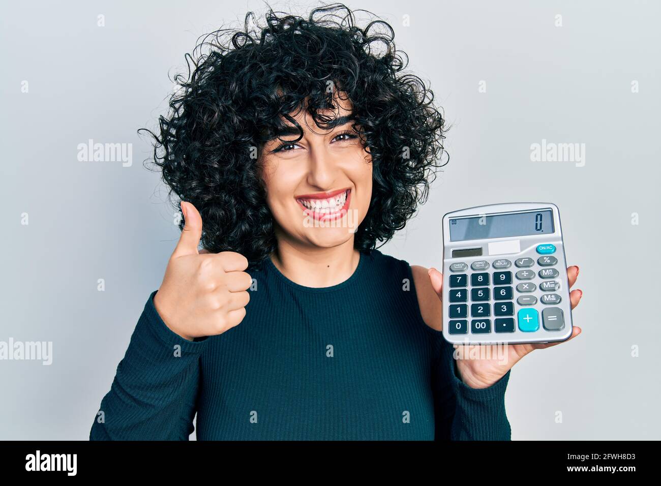 Young middle east woman showing calculator device smiling happy and ...