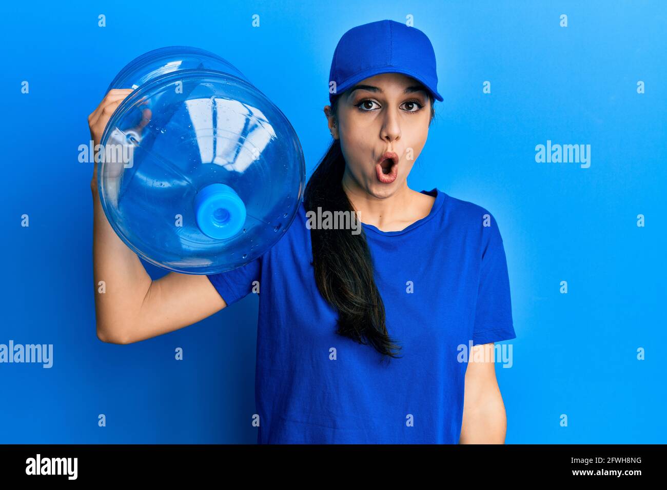 Young hispanic woman wearing delivery uniform holding water carafe ...