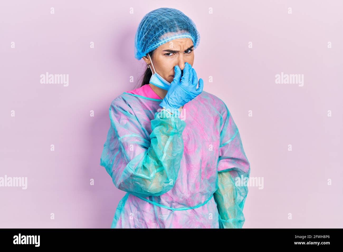 Young brunette woman wearing surgeon uniform and medical mask smelling ...