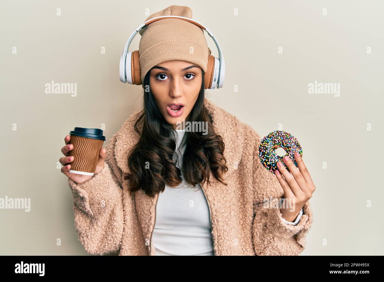 Young hispanic woman using headphones having breakfast in shock face ...
