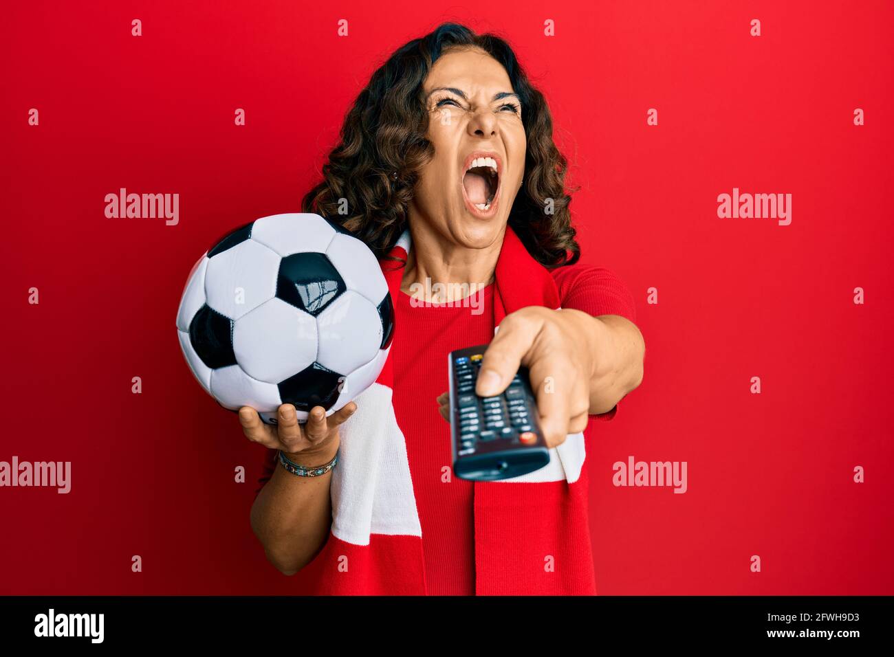 Middle age hispanic woman football hooligan holding ball using tv ...