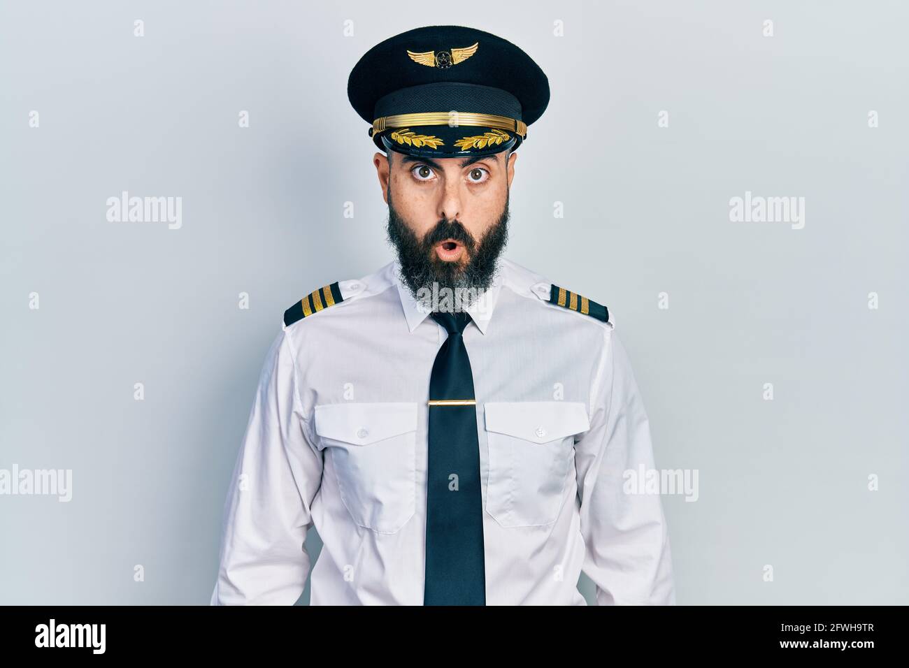 Young hispanic man wearing airplane pilot uniform afraid and shocked ...
