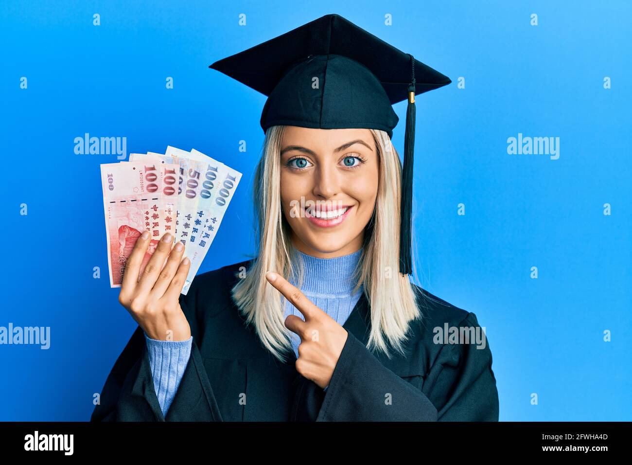 Beautiful blonde woman wearing graduation cap and ceremony robe holding ...