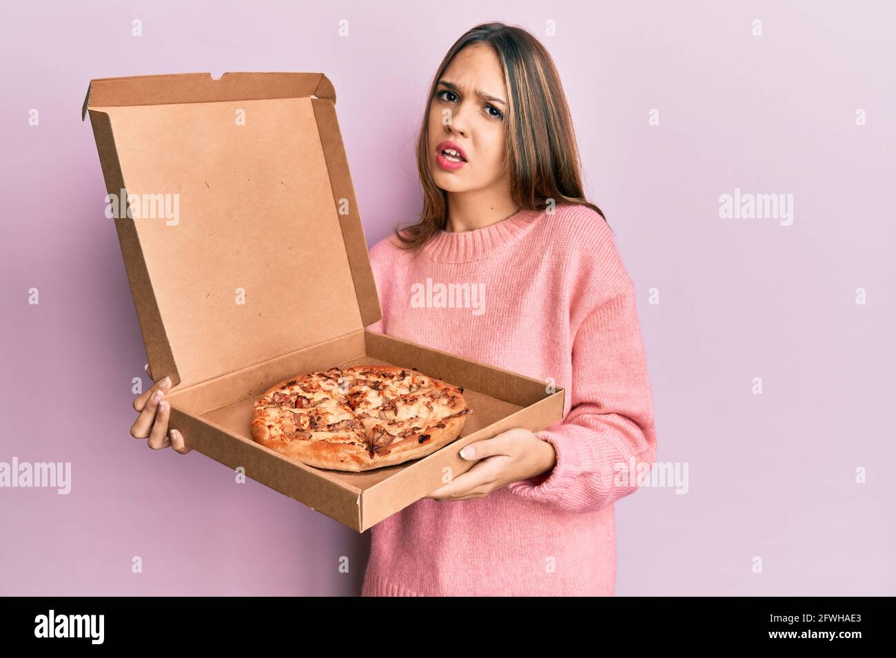 Young brunette woman holding italian pizza in shock face, looking ...