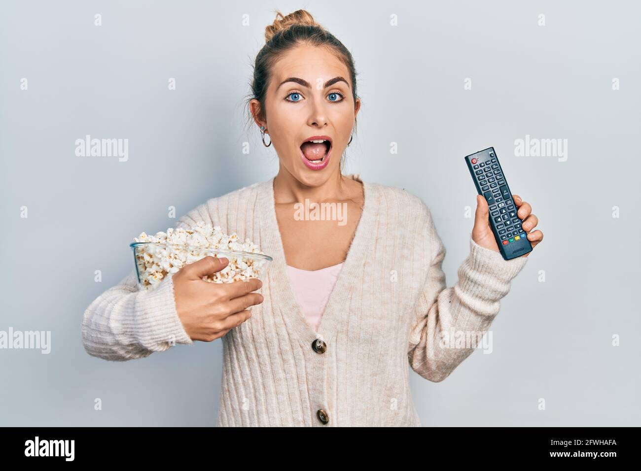 Young caucasian woman eating popcorn using tv control celebrating crazy ...
