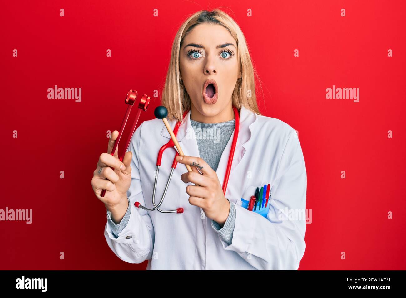 Young caucasian woman wearing doctor uniform holding tuning fork in ...