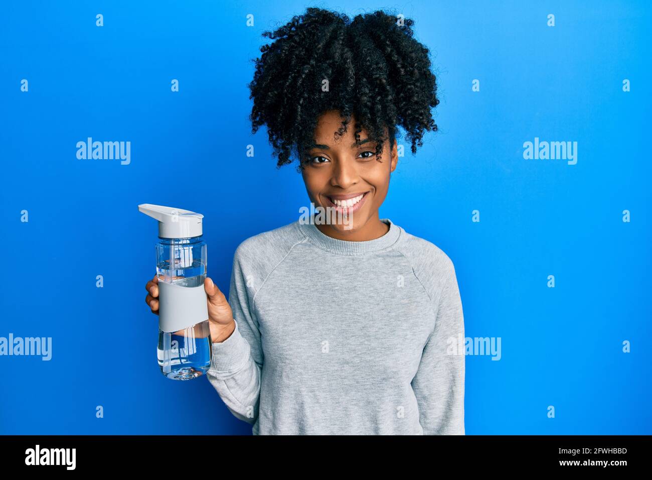African american woman with afro hair drinking bottle of water looking ...