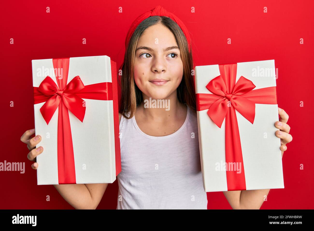 Beautiful brunette little girl holding gifts smiling looking to the ...