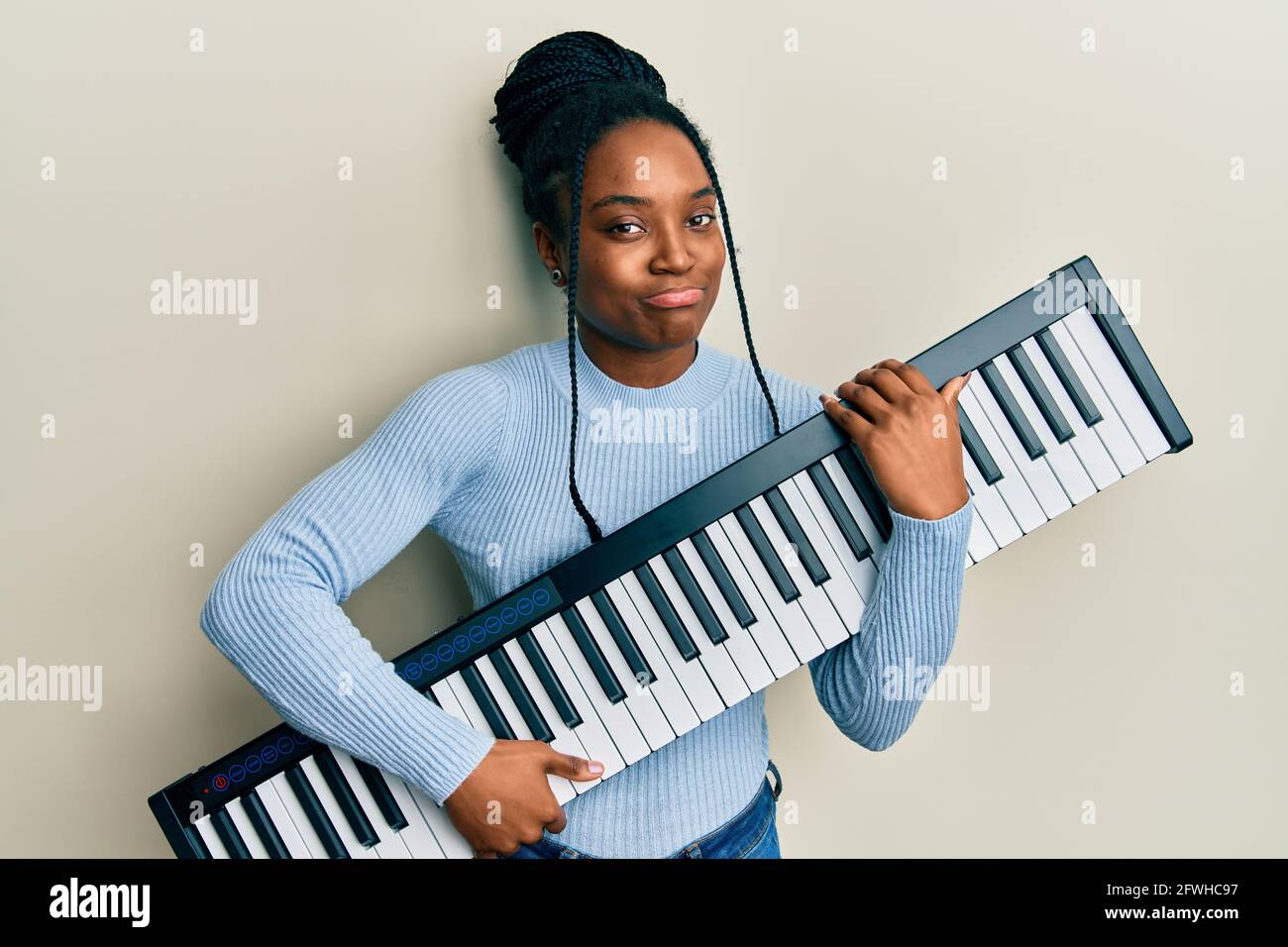 African american woman with braided hair holding piano keyboard ...