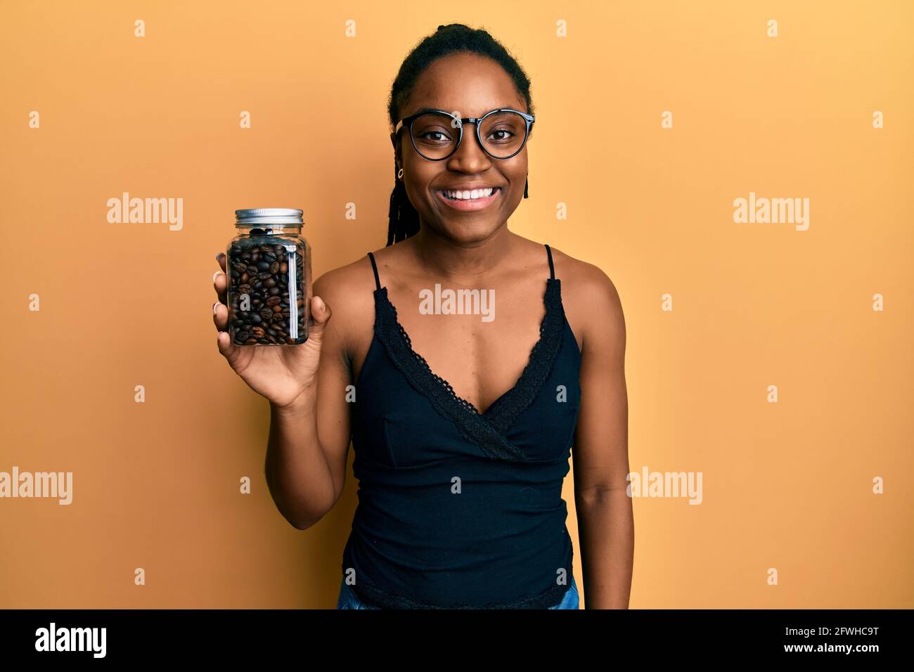 African american woman with braided hair holding jar with coffee beans ...