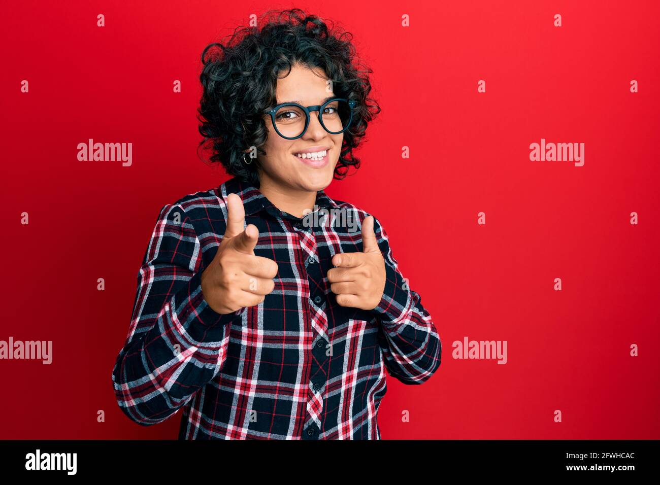 Young hispanic woman with curly hair wearing casual clothes and glasses ...