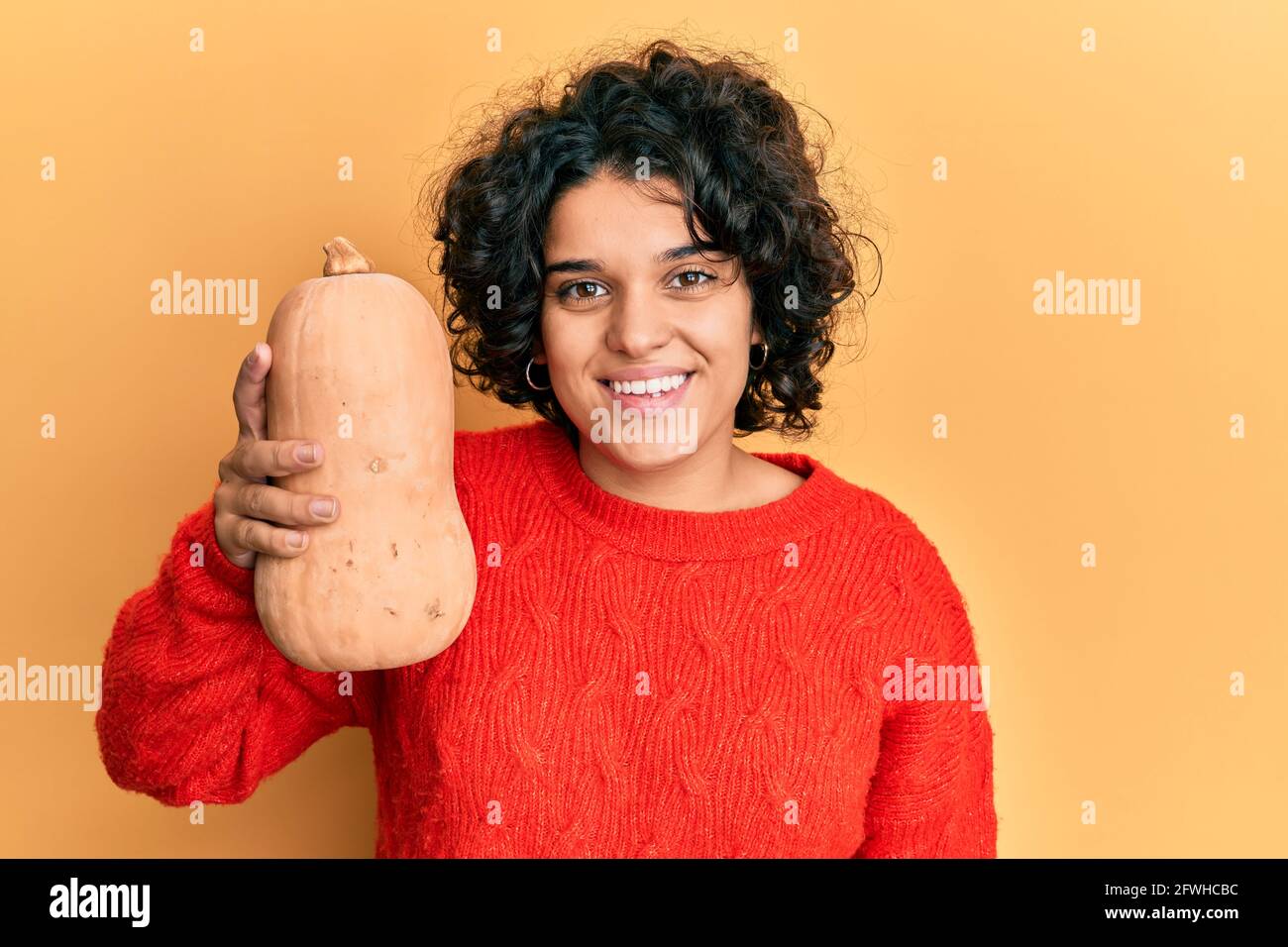 Young hispanic woman with curly hair holding fresh orange pumpkin ...