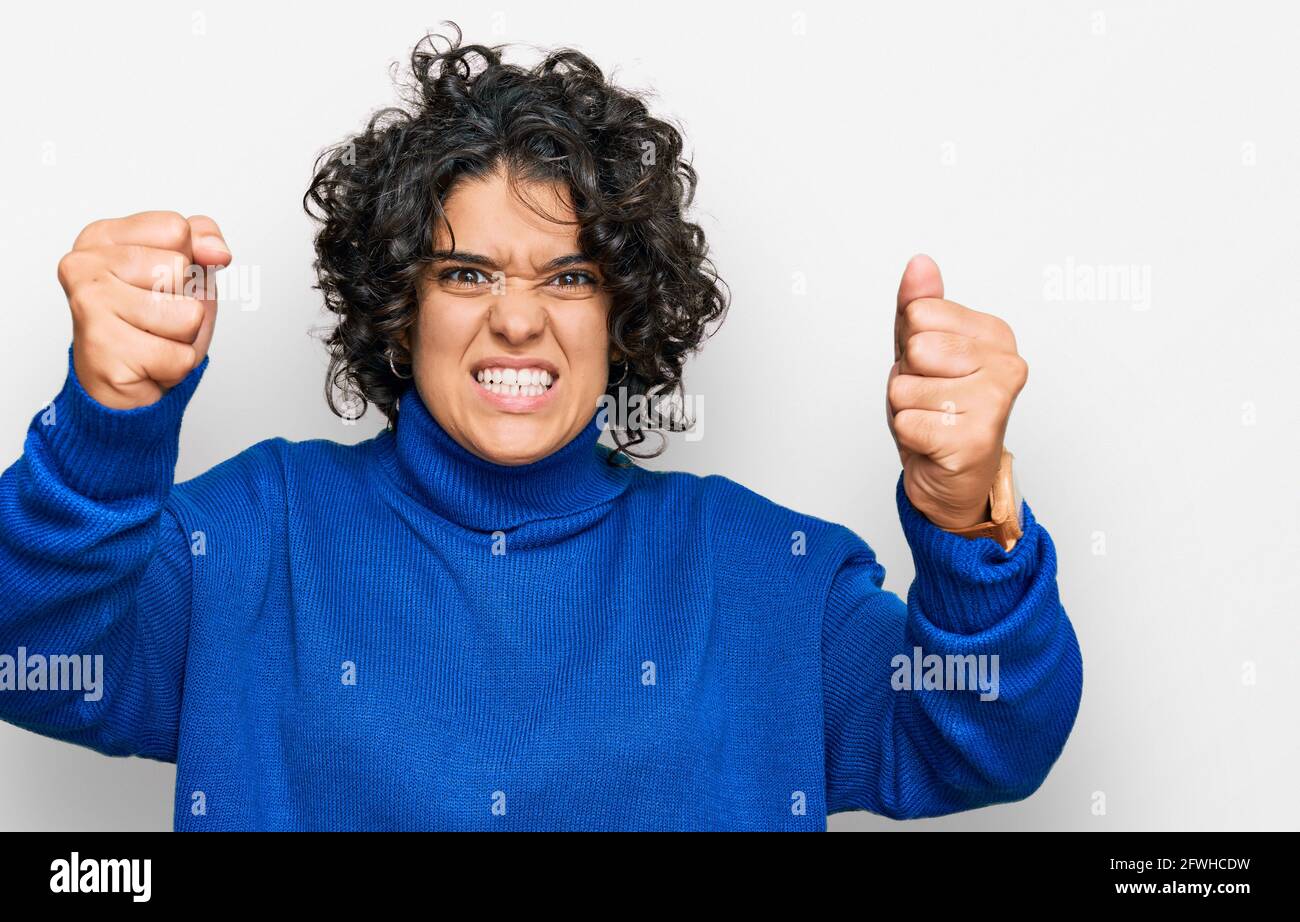 Young hispanic woman with curly hair wearing turtleneck sweater angry ...
