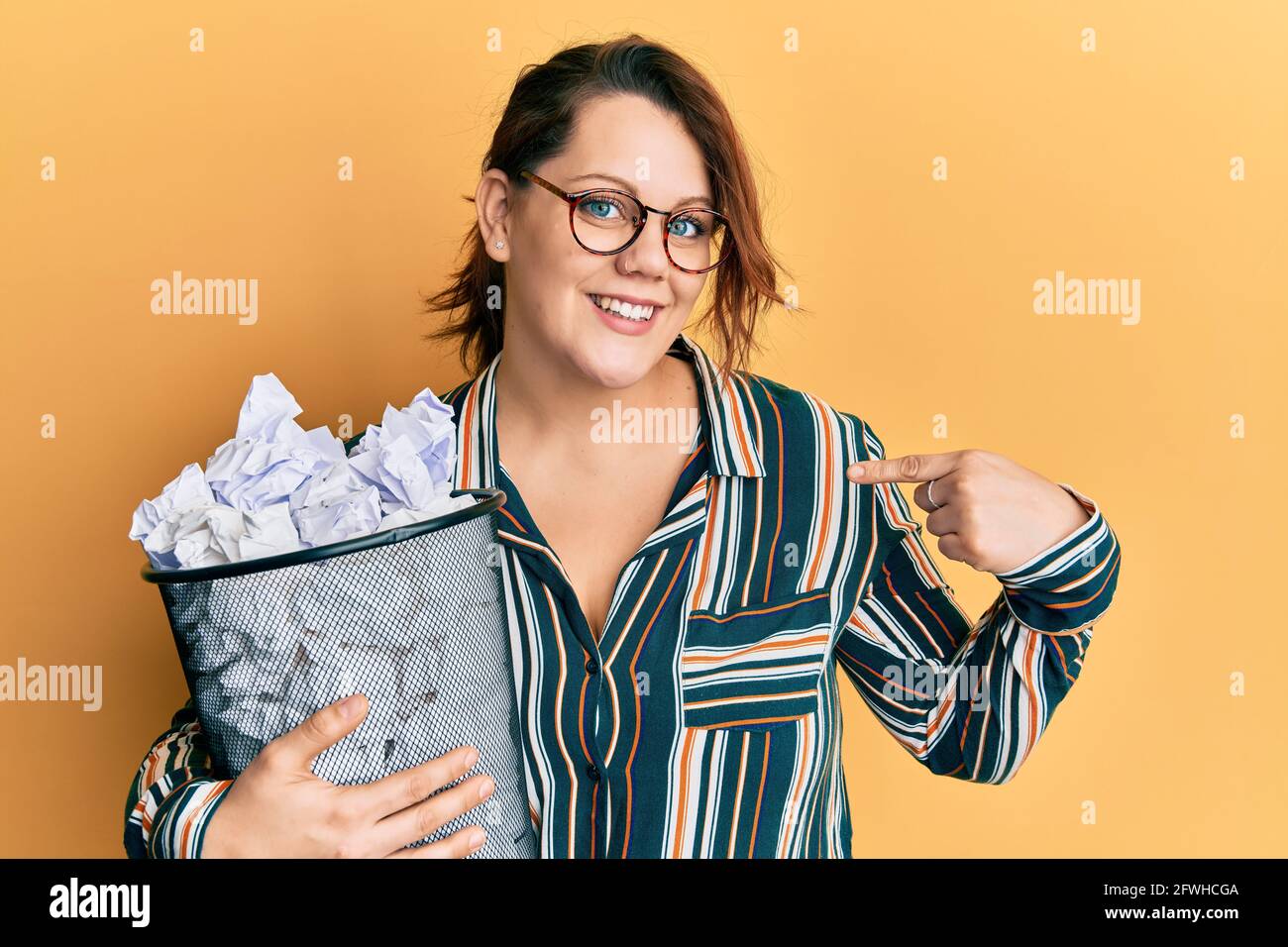 Young caucasian woman holding paper bin full of crumpled papers ...