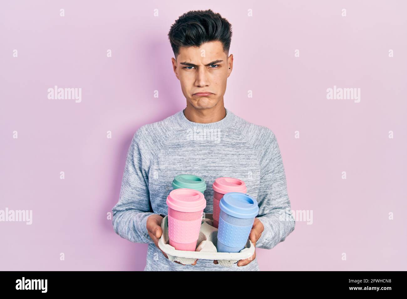Young hispanic man holding tray with take away coffee depressed and ...